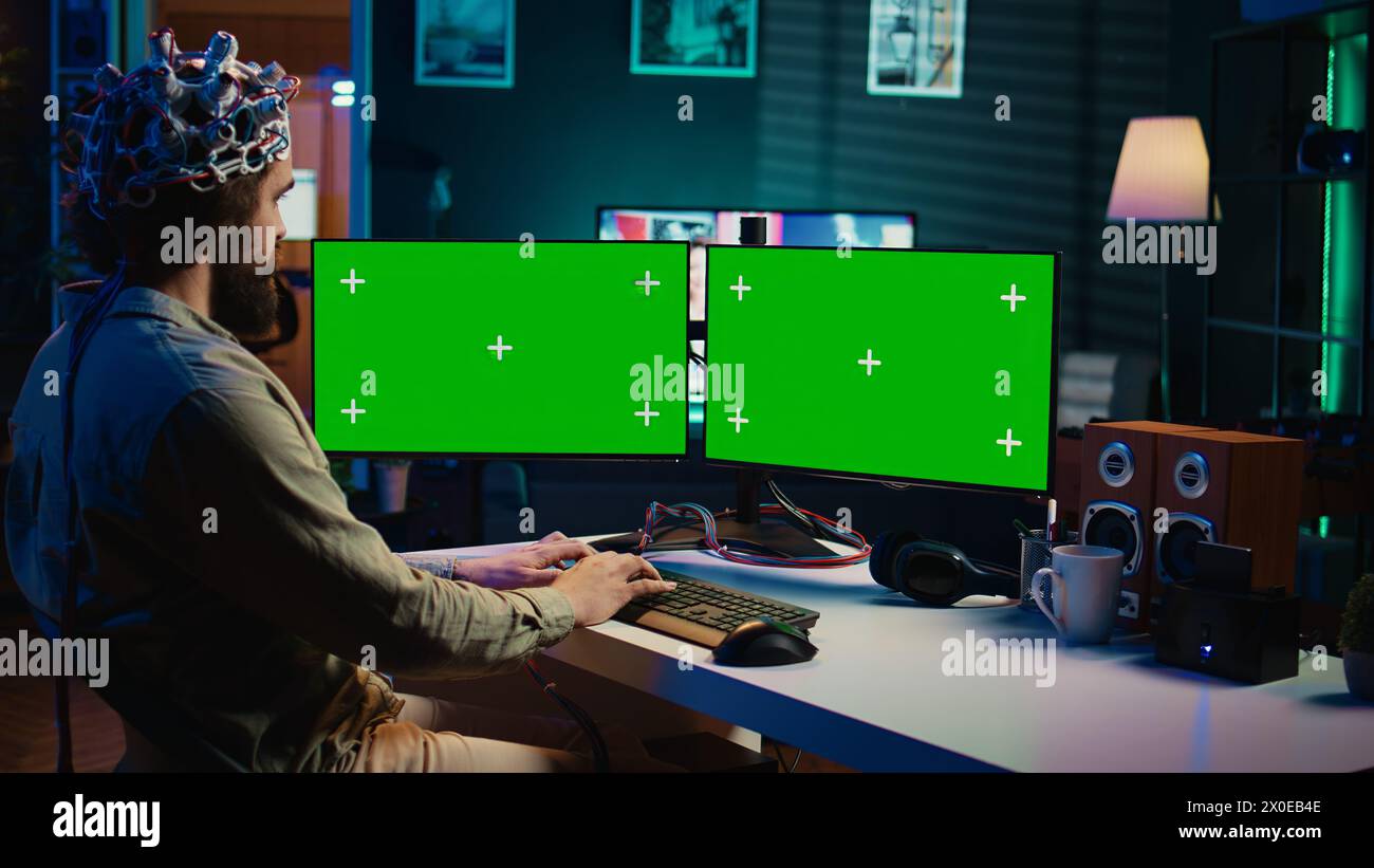 Computer engineer using EEG headset, starting mind upload process using green screen PC. Man ...