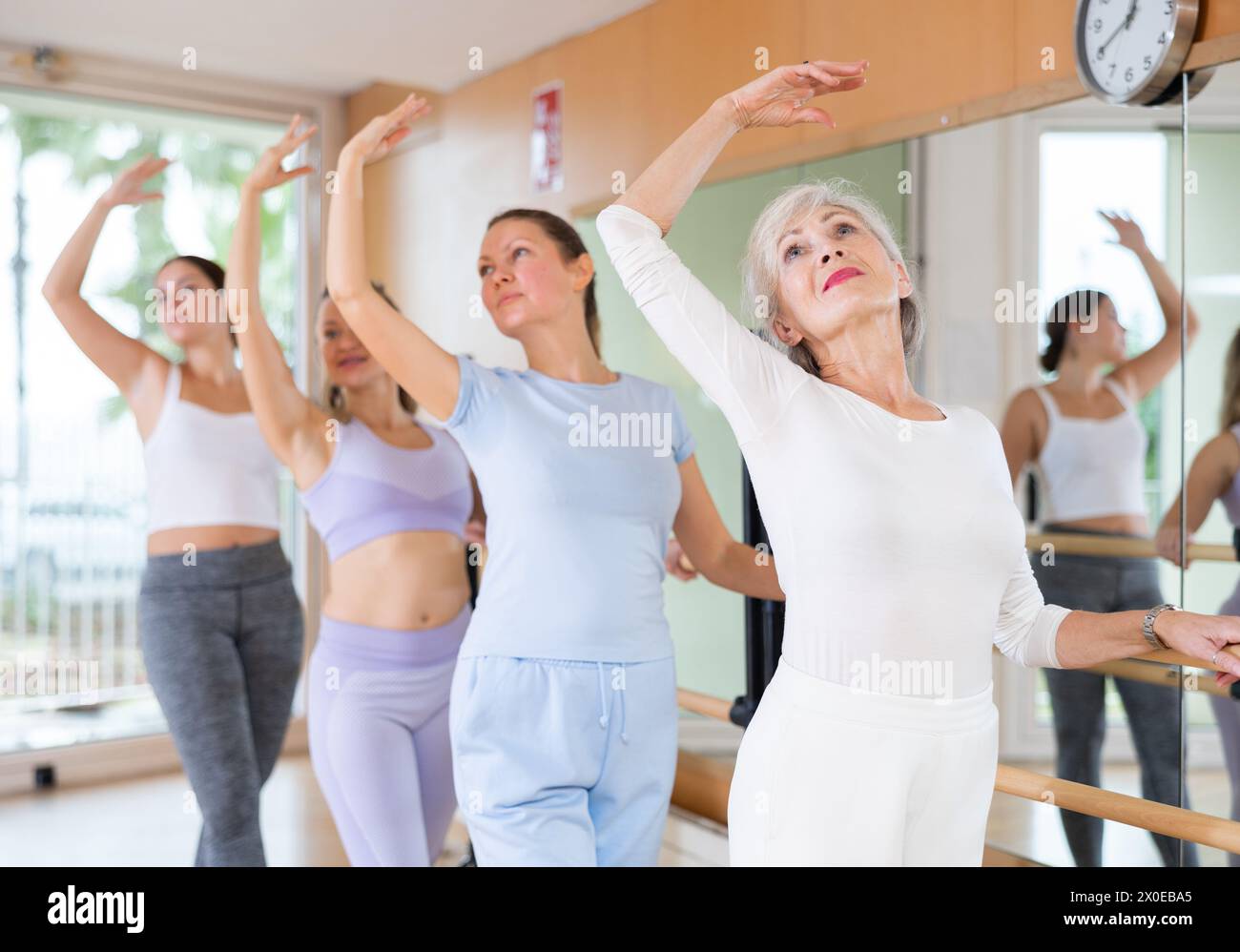 Mature female instructor showing position near barre for small class of ...