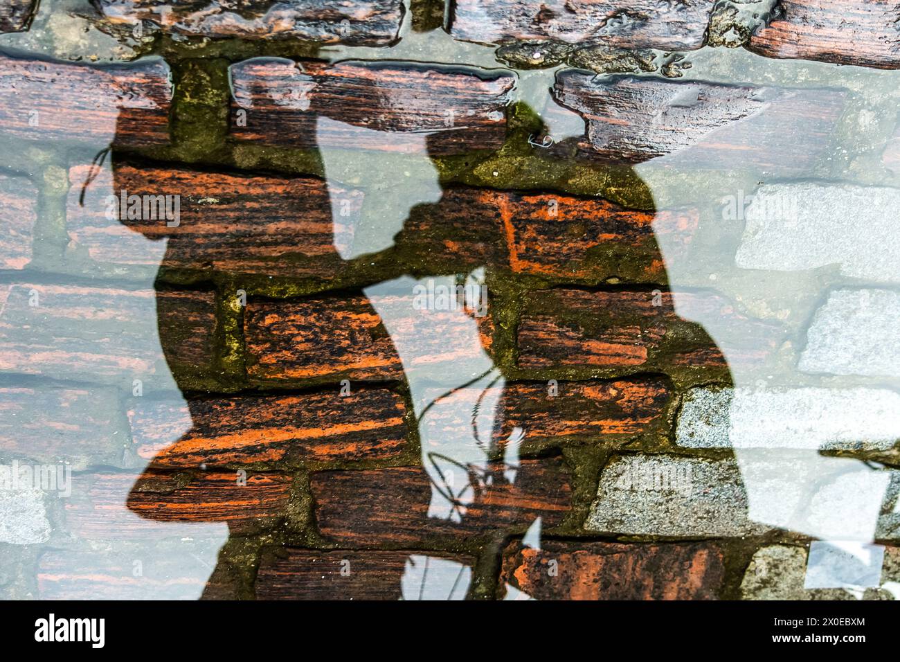 Reflection of person and bicycle in a puddle of rainwater in the river ...