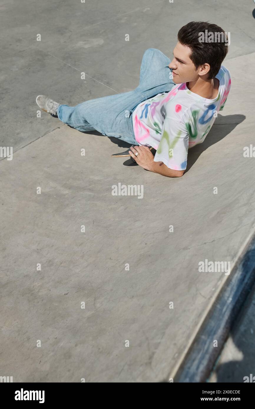 A man in casual attire lounging on the ground next to his skateboard ...