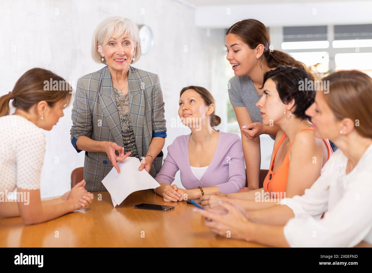 Women discuss documents sitting at table in office Stock Photo - Alamy