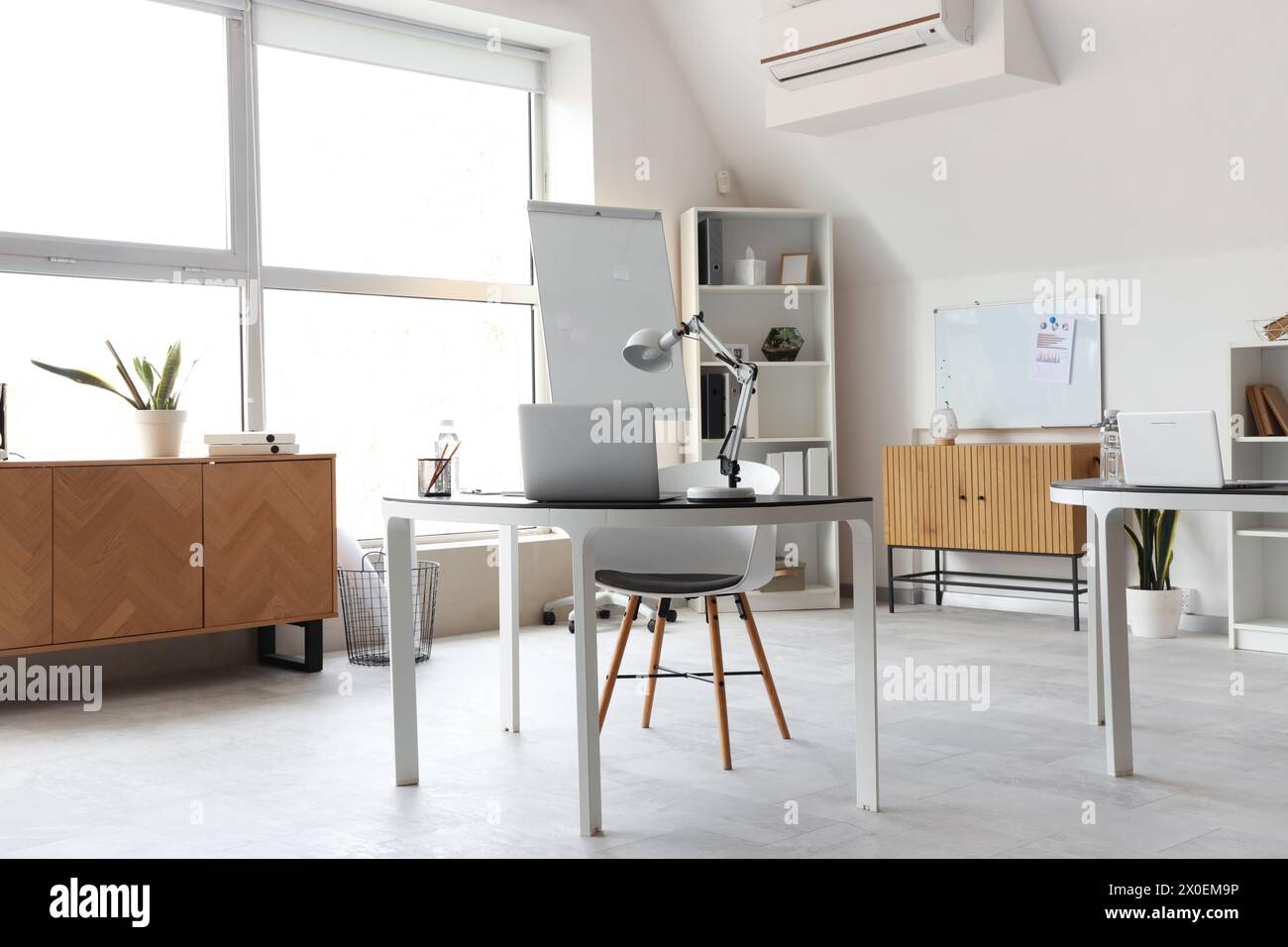 Interior of light office with shelving unit, chest of drawers, tables ...