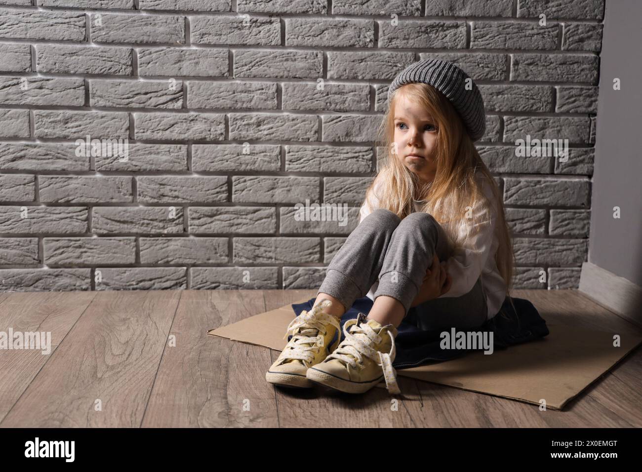 homeless little girl sitting on floor near grey brick wall Stock Photo ...