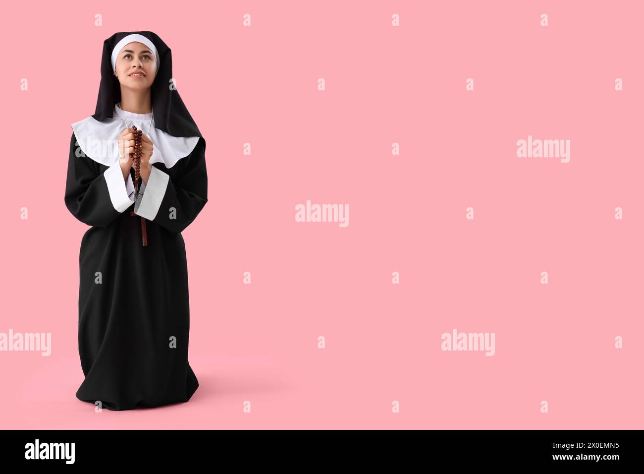 Young nun with beads praying on pink background Stock Photo - Alamy