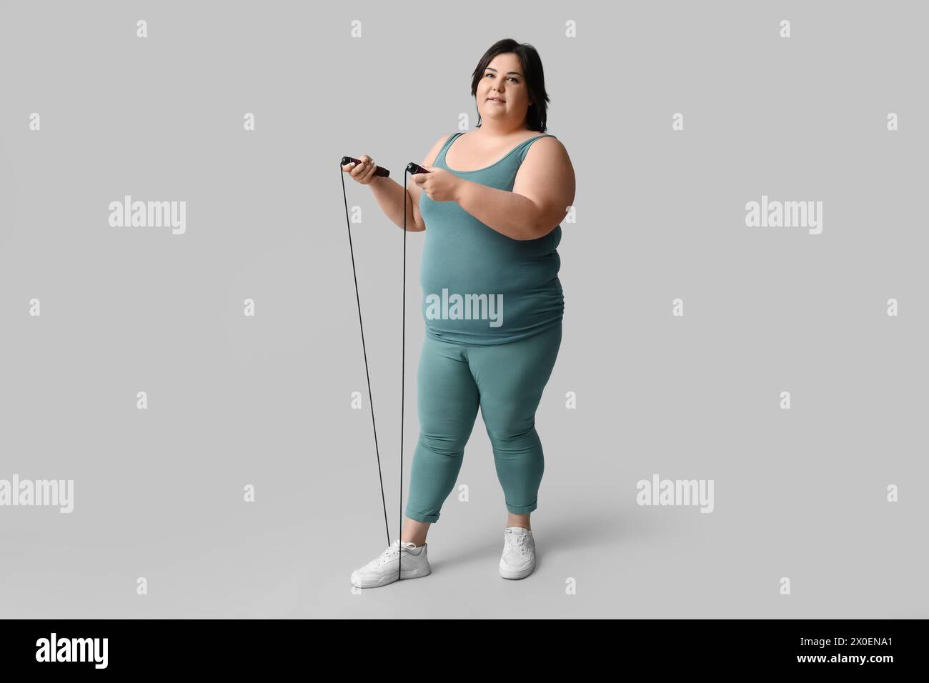 Happy young overweight woman with jumping rope on grey background ...
