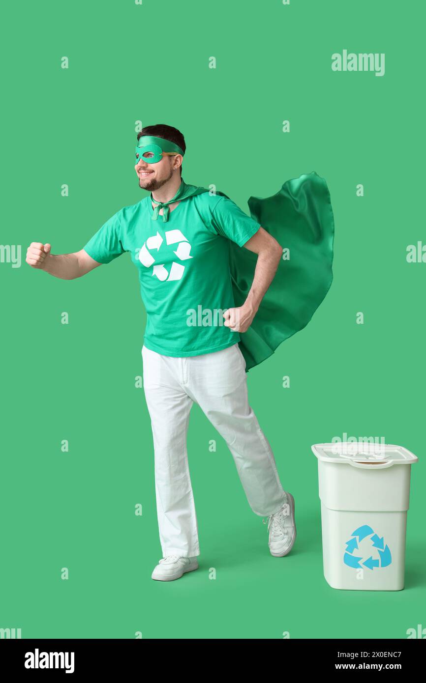 Young man dressed as eco superhero with garbage bin running on green ...