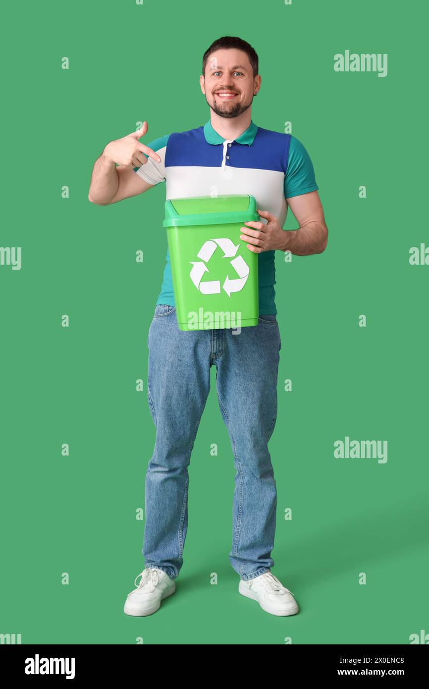 Happy young man pointing at trash bin with recycling logo on green ...