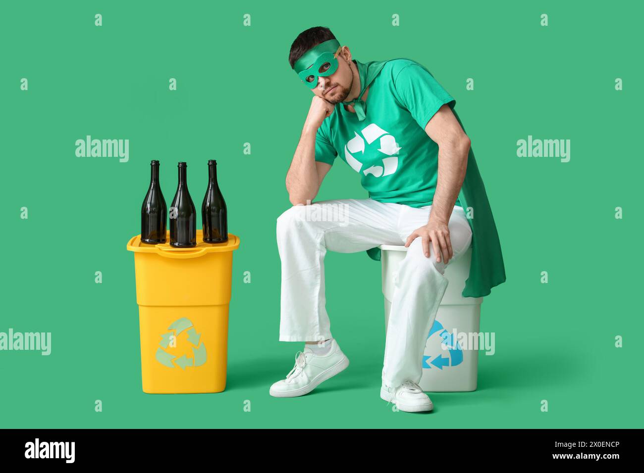 Tired young man dressed as eco superhero sitting on garbage bin with ...
