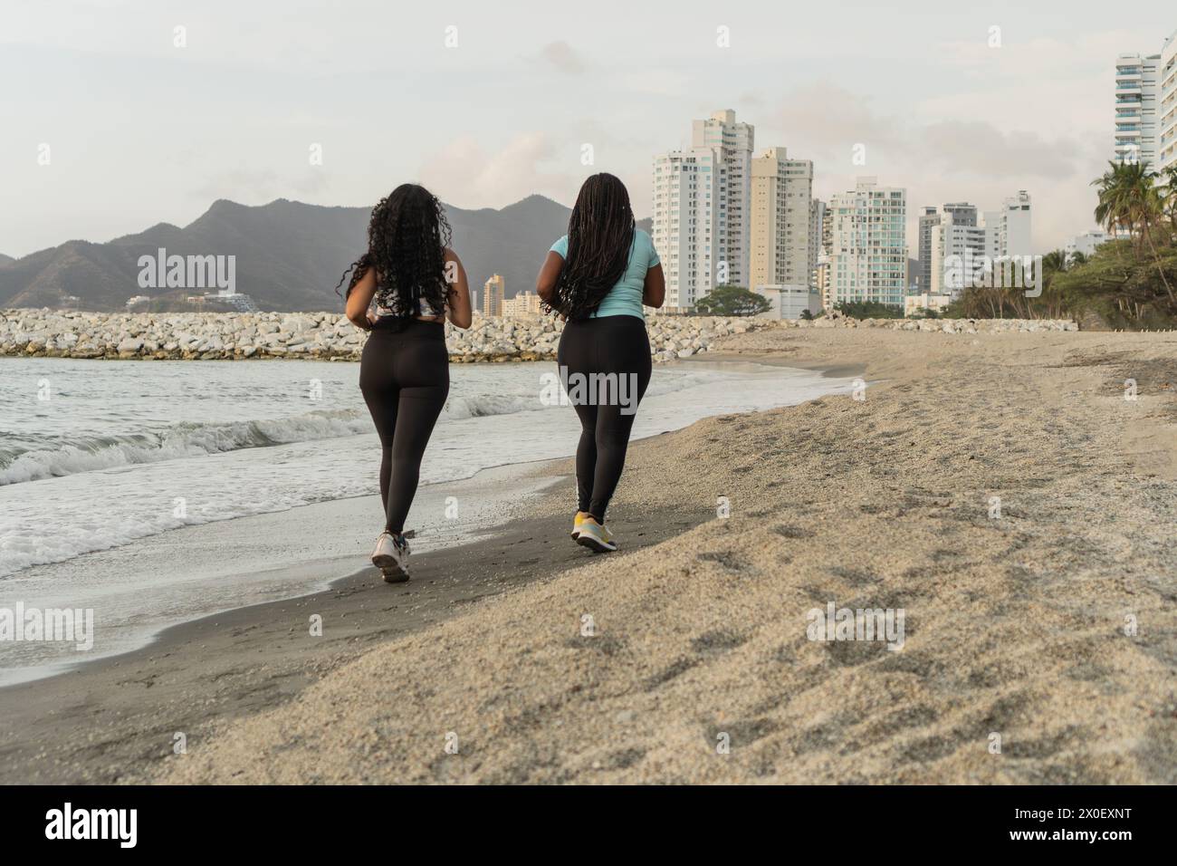 Two women running on a beach with the city skyline in the background ...