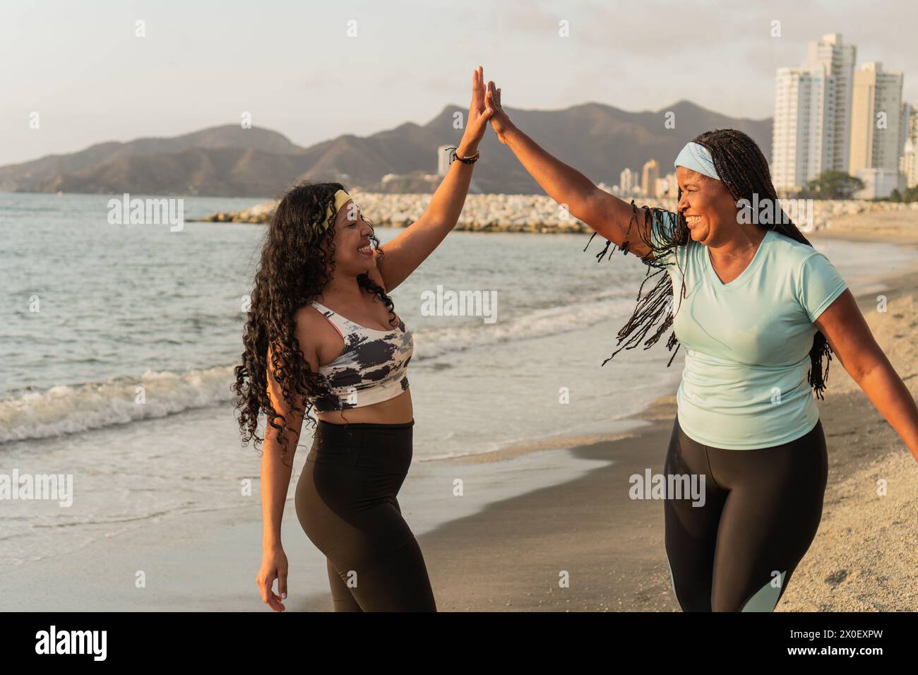 Latin women high-five during a beach workout, celebrating their fitness ...