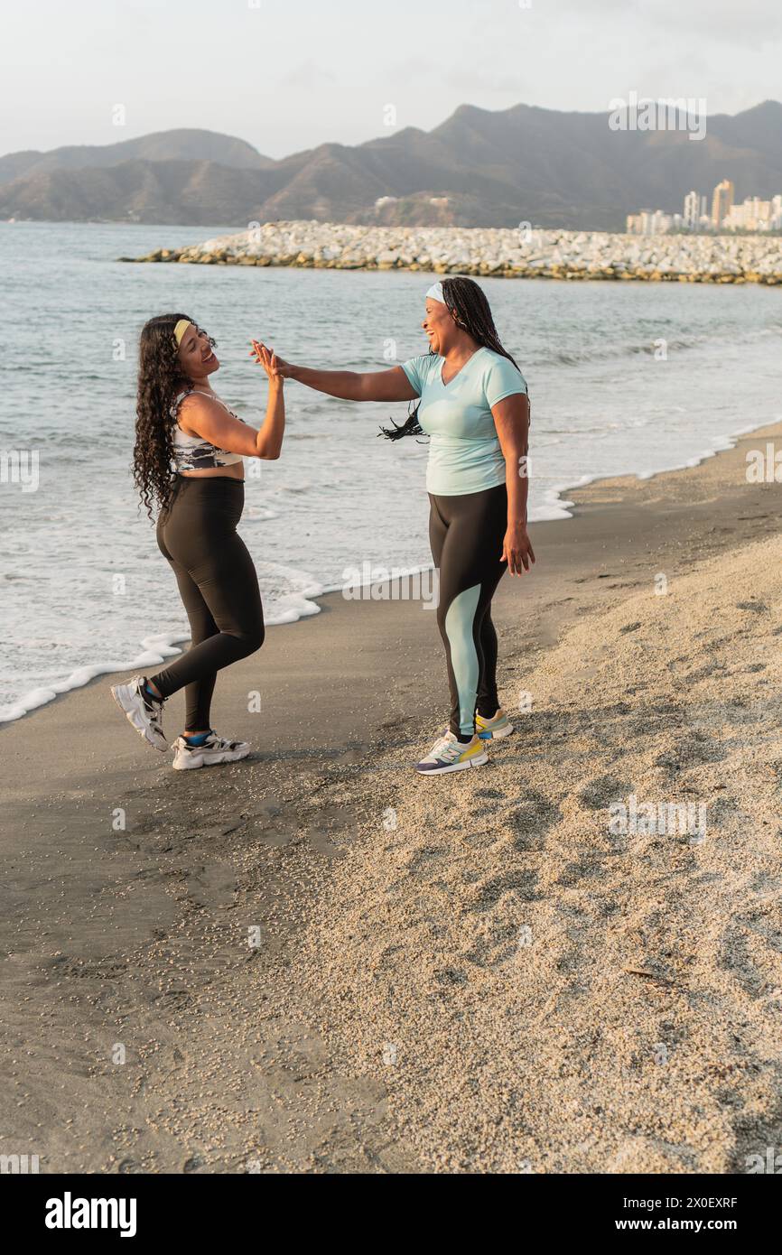 Two joyful women high-five during a beach workout, celebrating their ...