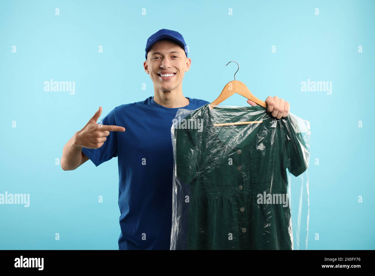 Dry-cleaning delivery. Happy courier holding dress in plastic bag on ...