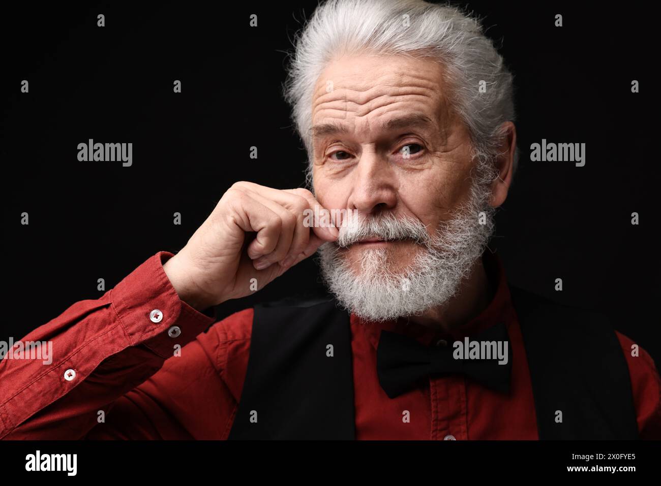 Senior man touching mustache on black background Stock Photo - Alamy