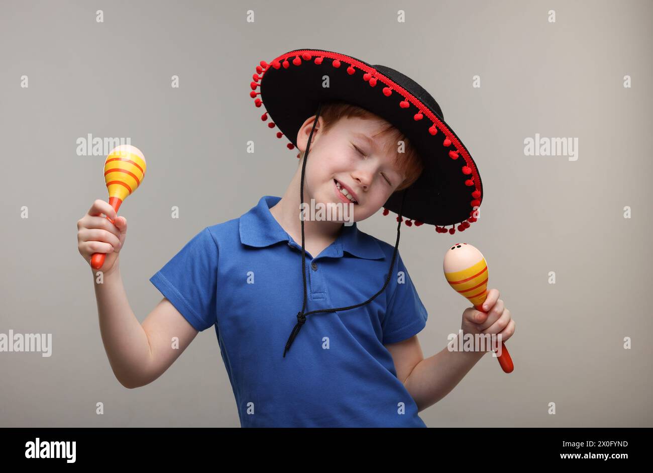 Cute boy in Mexican sombrero hat with maracas dancing on grey ...