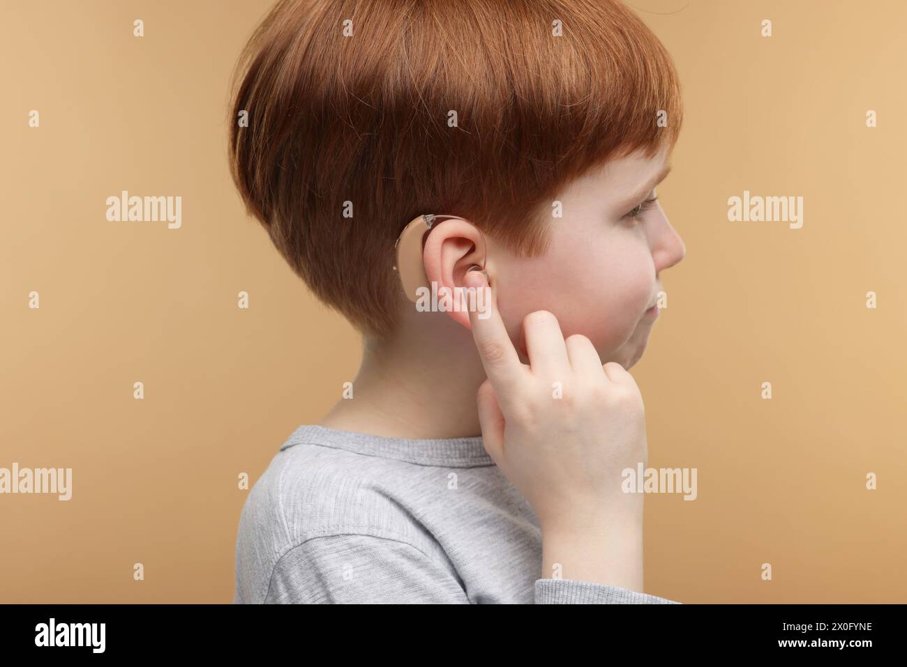 Little boy with hearing aid on pale brown background Stock Photo - Alamy