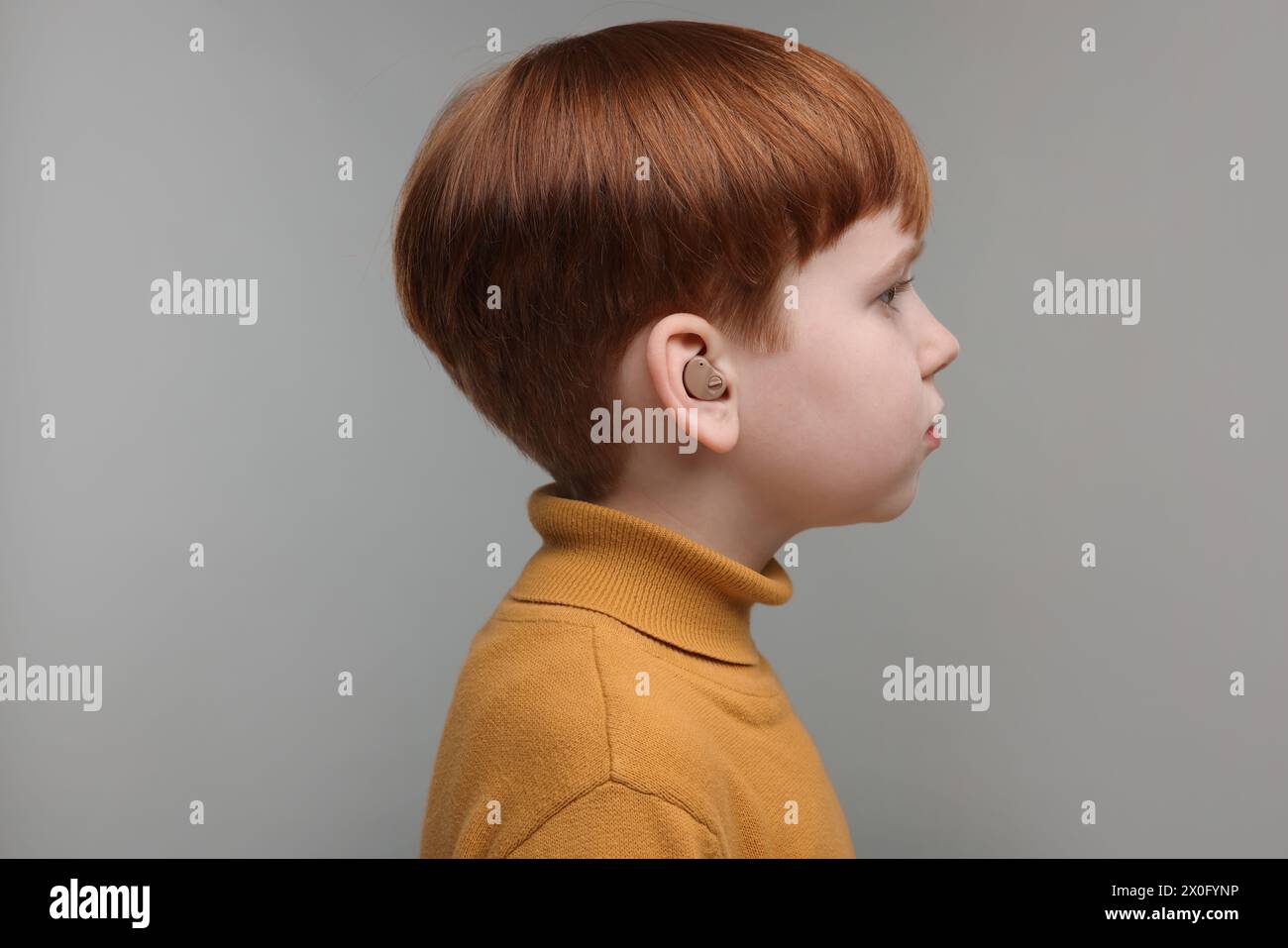 Little boy with hearing aid on grey background Stock Photo - Alamy
