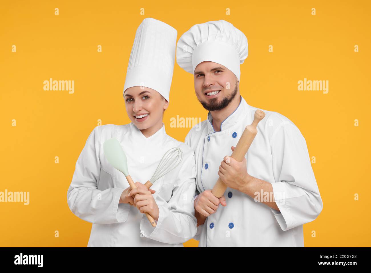 Happy confectioners in uniforms holding professional tools on yellow ...
