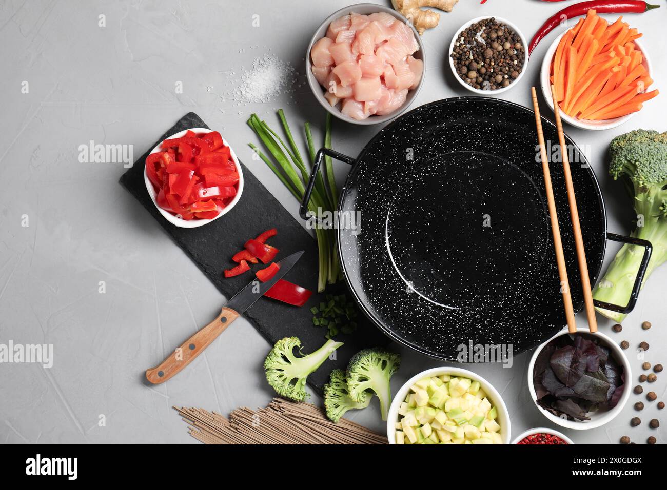 Wok pan, noodles, chicken and other products on light grey table, flat ...