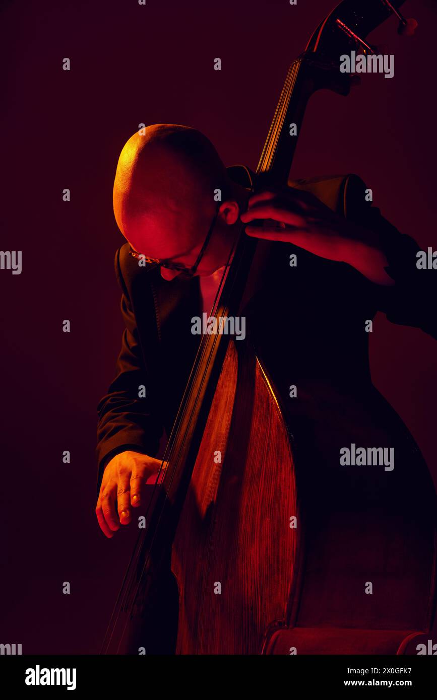 Portrait of bald musician in glasses plays double bass in red-yellow ...
