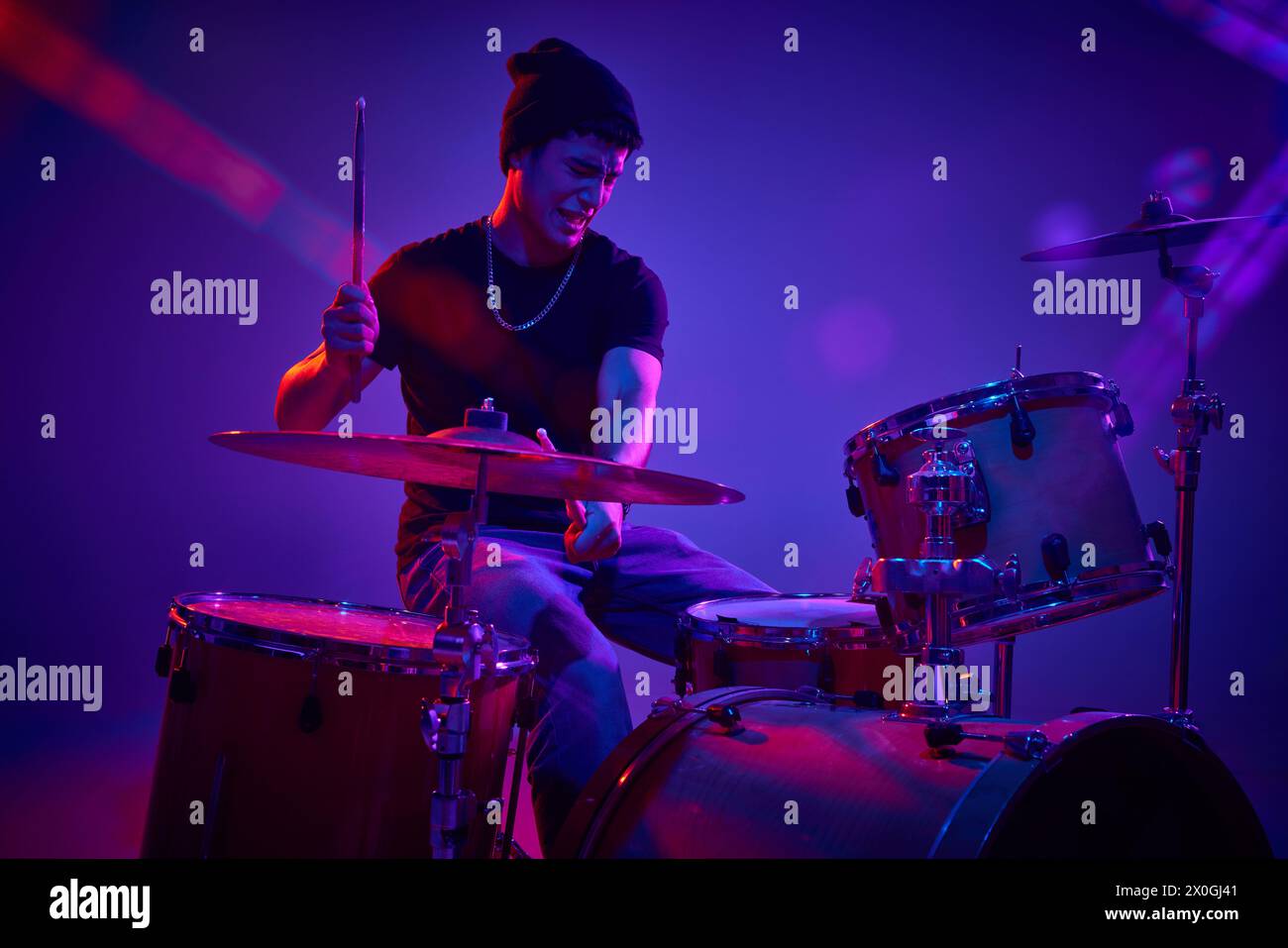 Talented drummer in casual attire practices in pink-purple stage ...