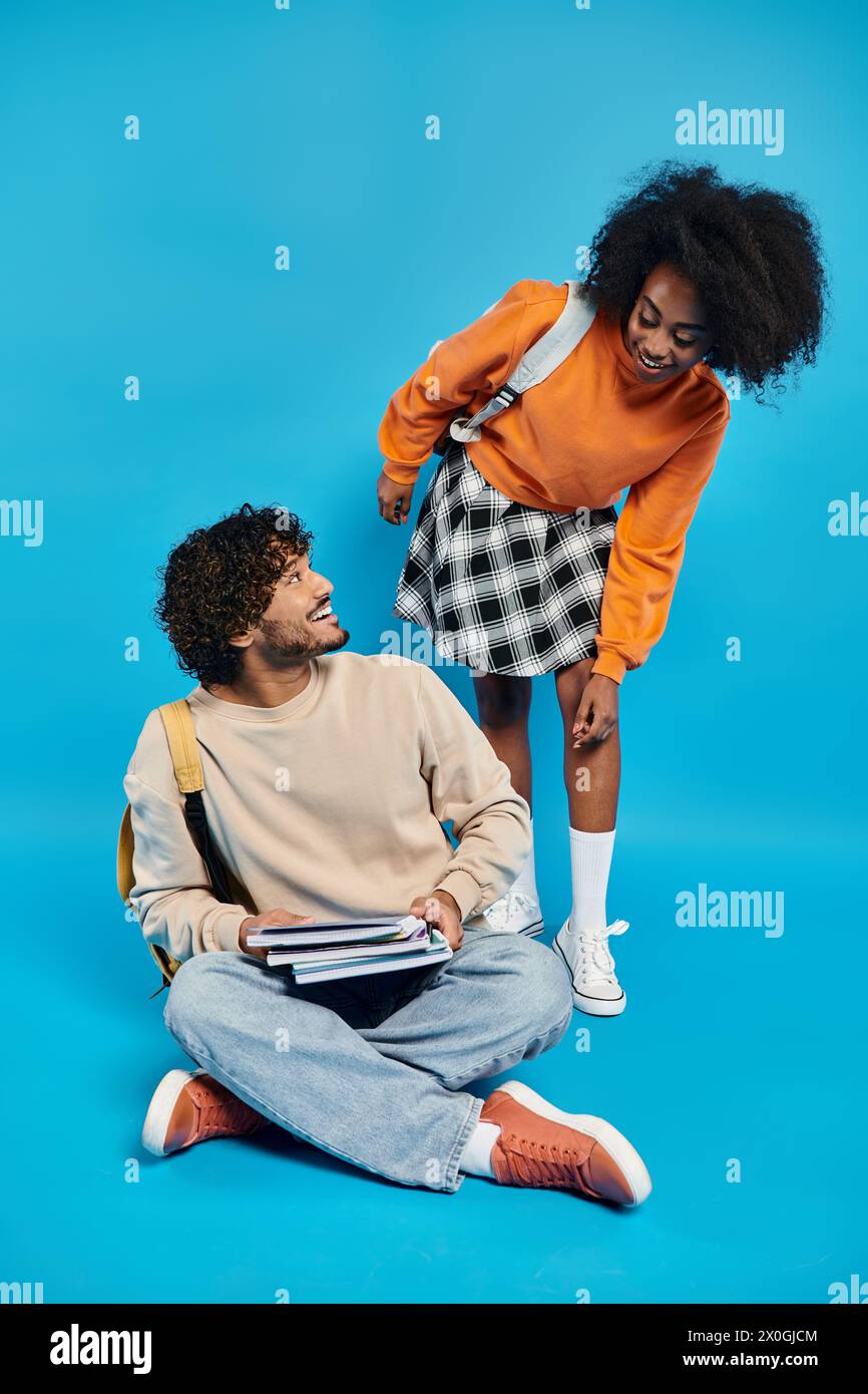 A pair of interracial students sit side by side on the ground, engaged ...
