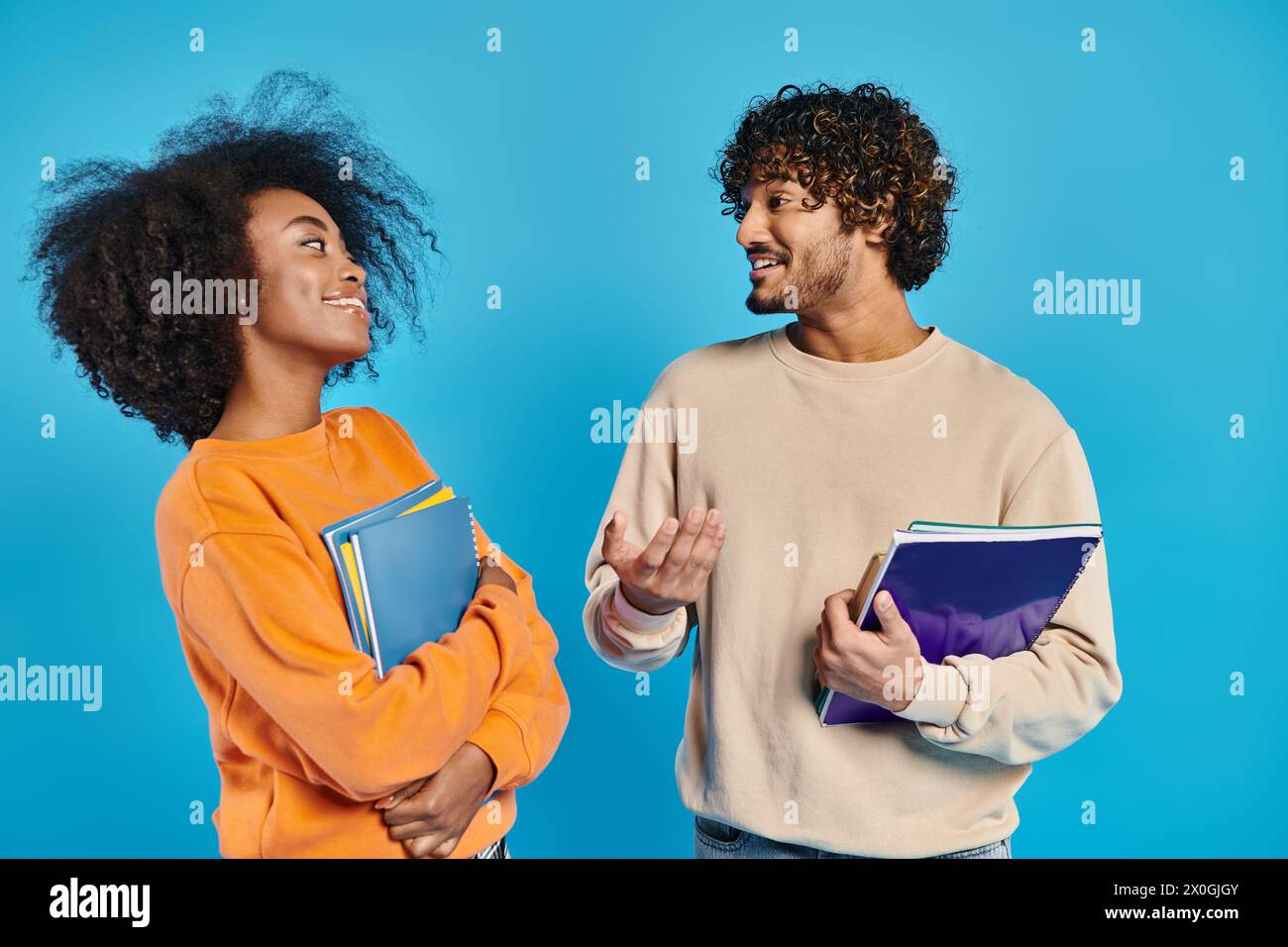 Two interracial students stand closely on a blue backdrop in a studio ...