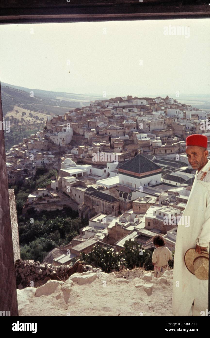 A Moroccan man wearing a traditional fez hat in front of the tomb of ...