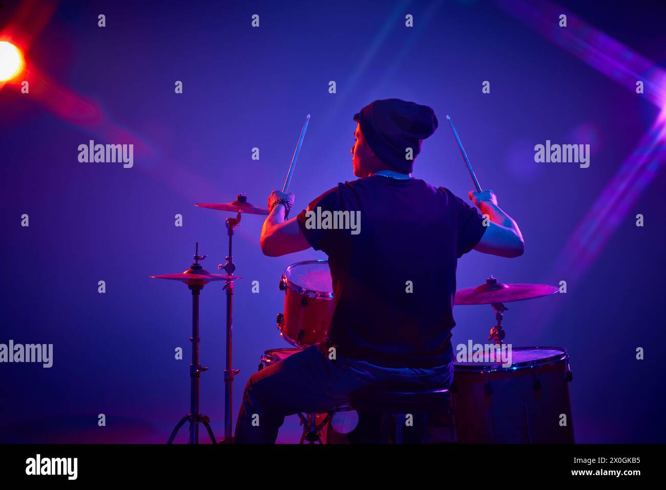 Rear view portrait of young artistic drummer performing in pink-purple ...