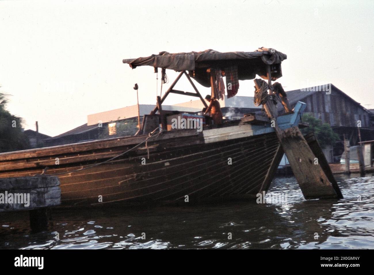 Man is steering a barge on a Khlong in Bangkok. [automated translation ...