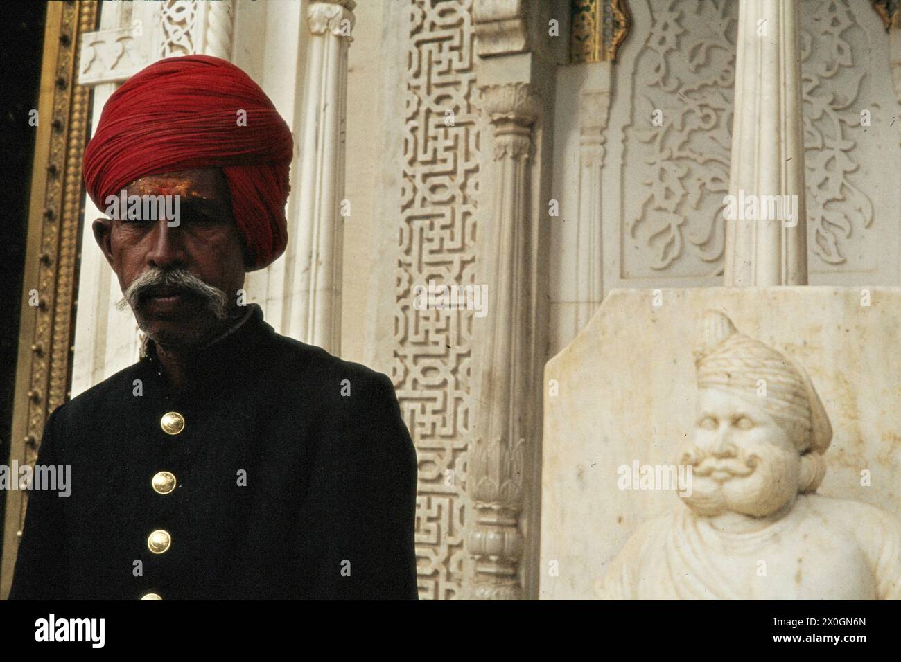 Guard in historical costume with red turban next to a statue in front ...