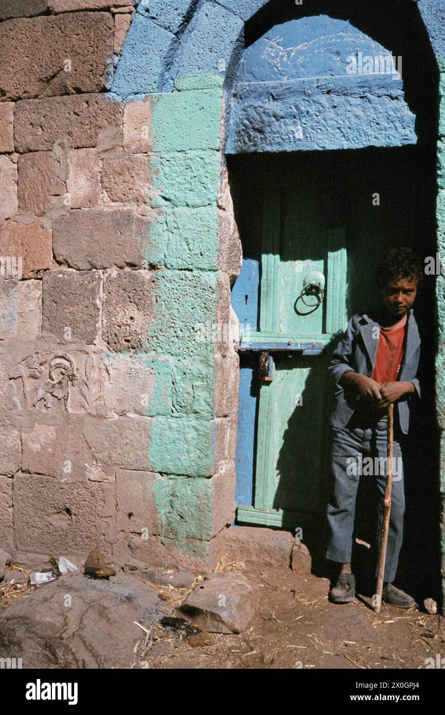 A Yemeni boy with a cane stands in a house entrance in Safar with a ...