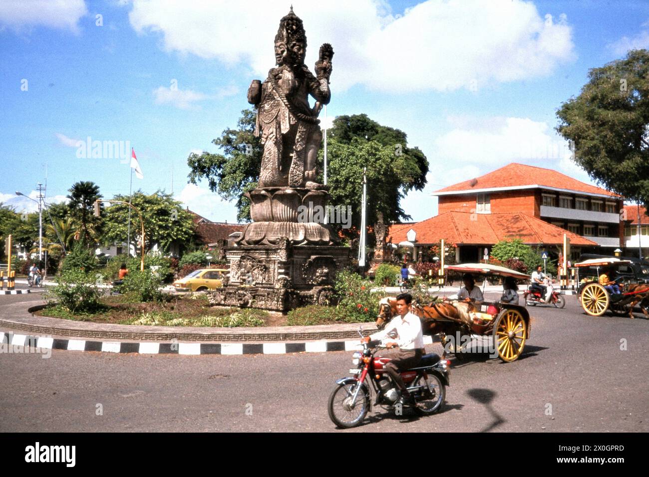 The statue of a guard stands on an island in a roundabout in Denpasar ...