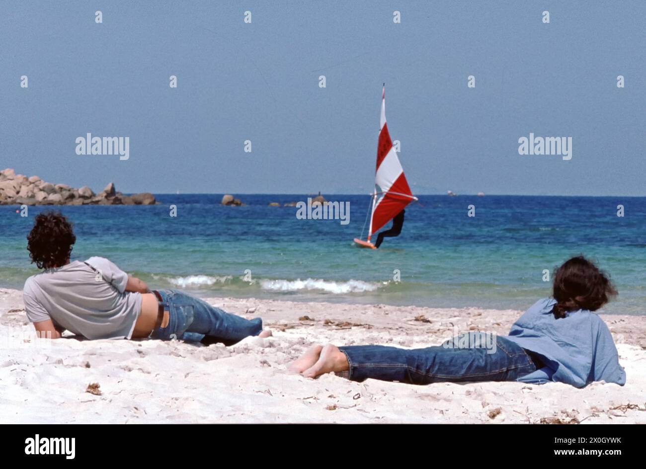 A young woman and a young man lie on the beach in Corsica and watch a ...