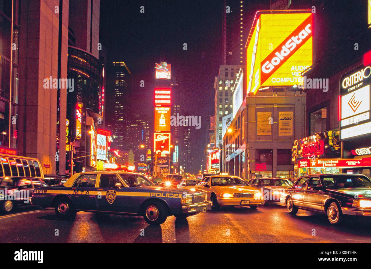 Times Square with neon signs at night. In the foreground a police car ...