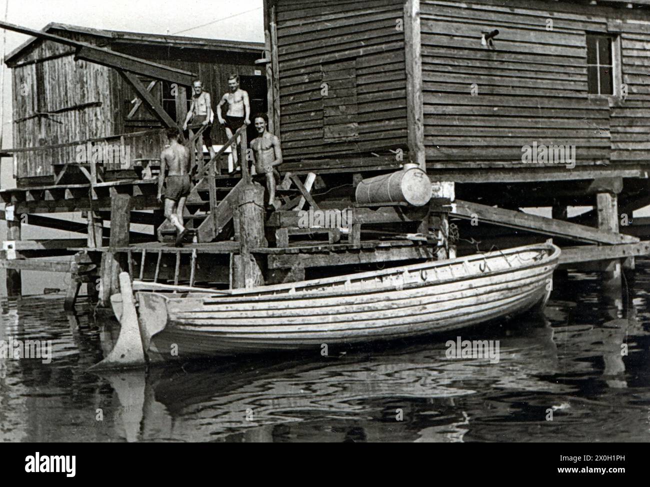 Young men with bathing trunks in front of a boathouse with rowboat ...