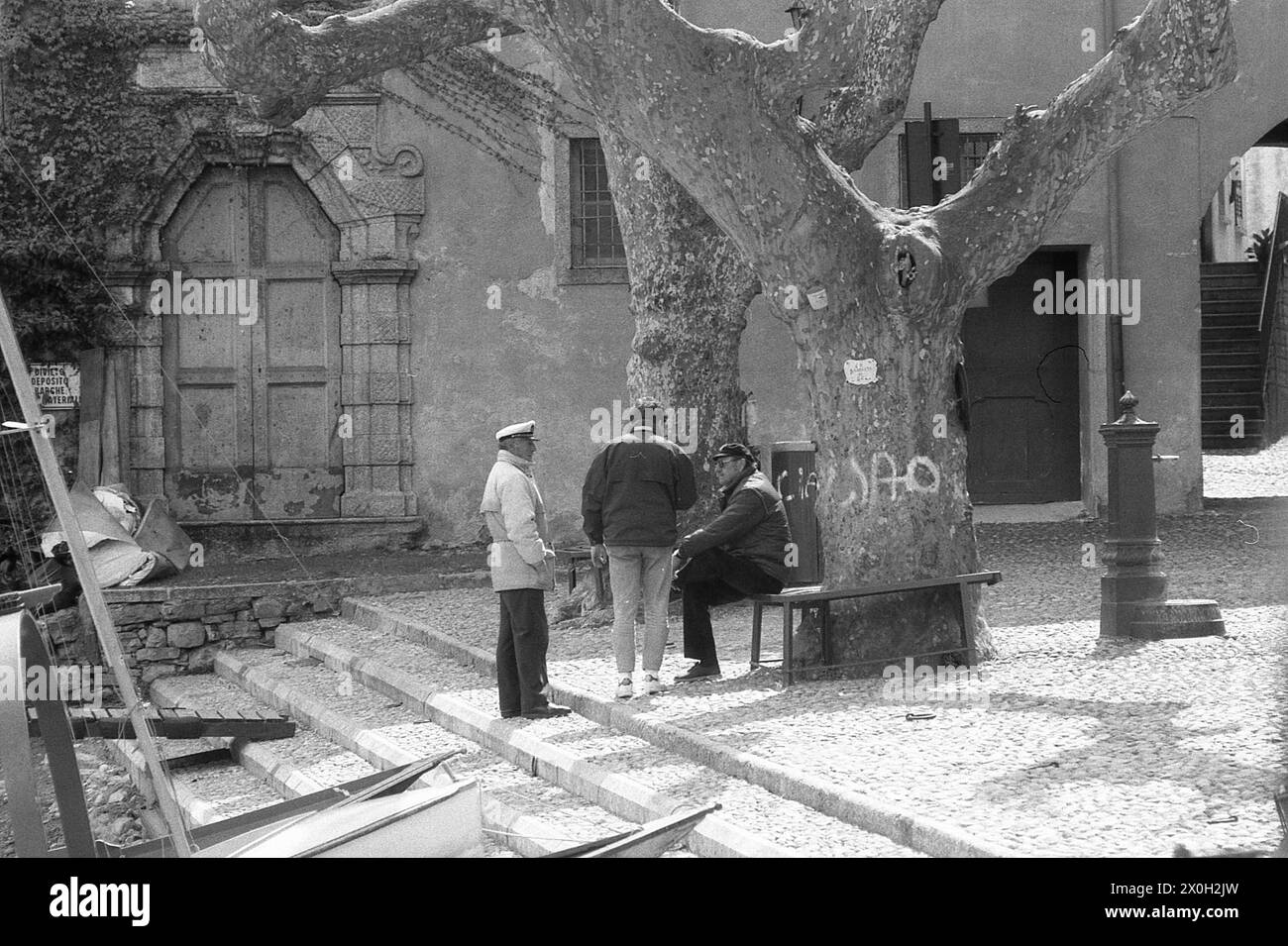 Three men, one with cap, chat in a port town on Lake Como Stock Photo ...