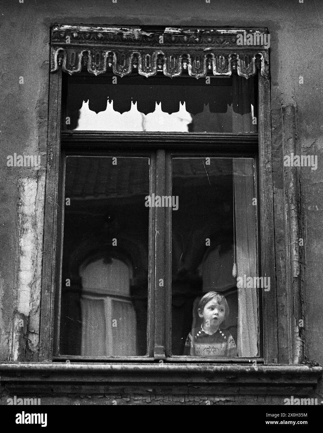 A child looks curiously out of a window of a residential building ...