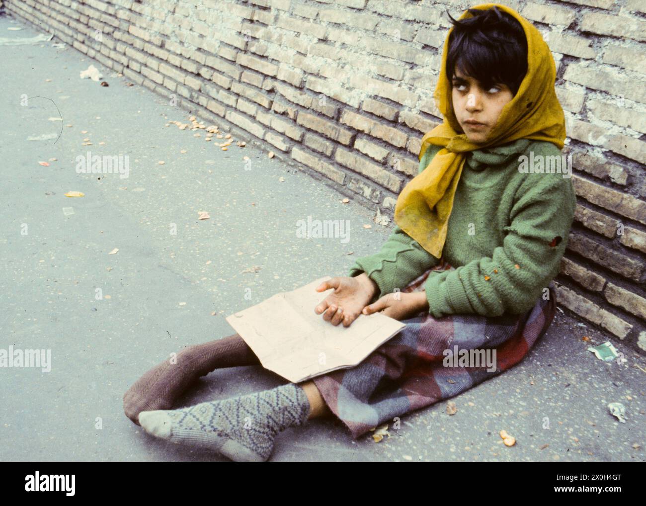 A begging, ragged girl sits on the side of the road and begs for money ...