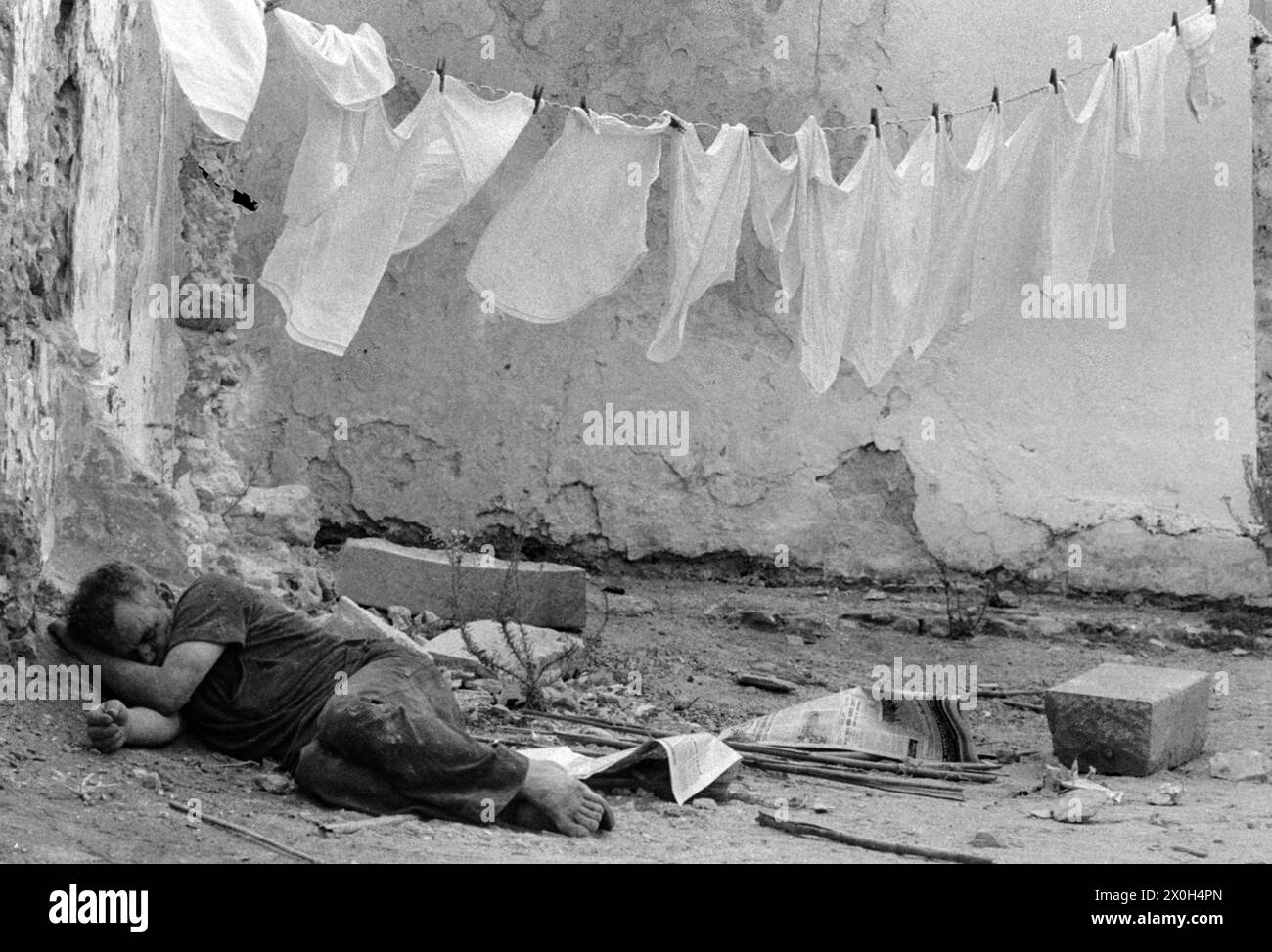 Under the freshly washed laundry flapping on the line, a drunk is ...