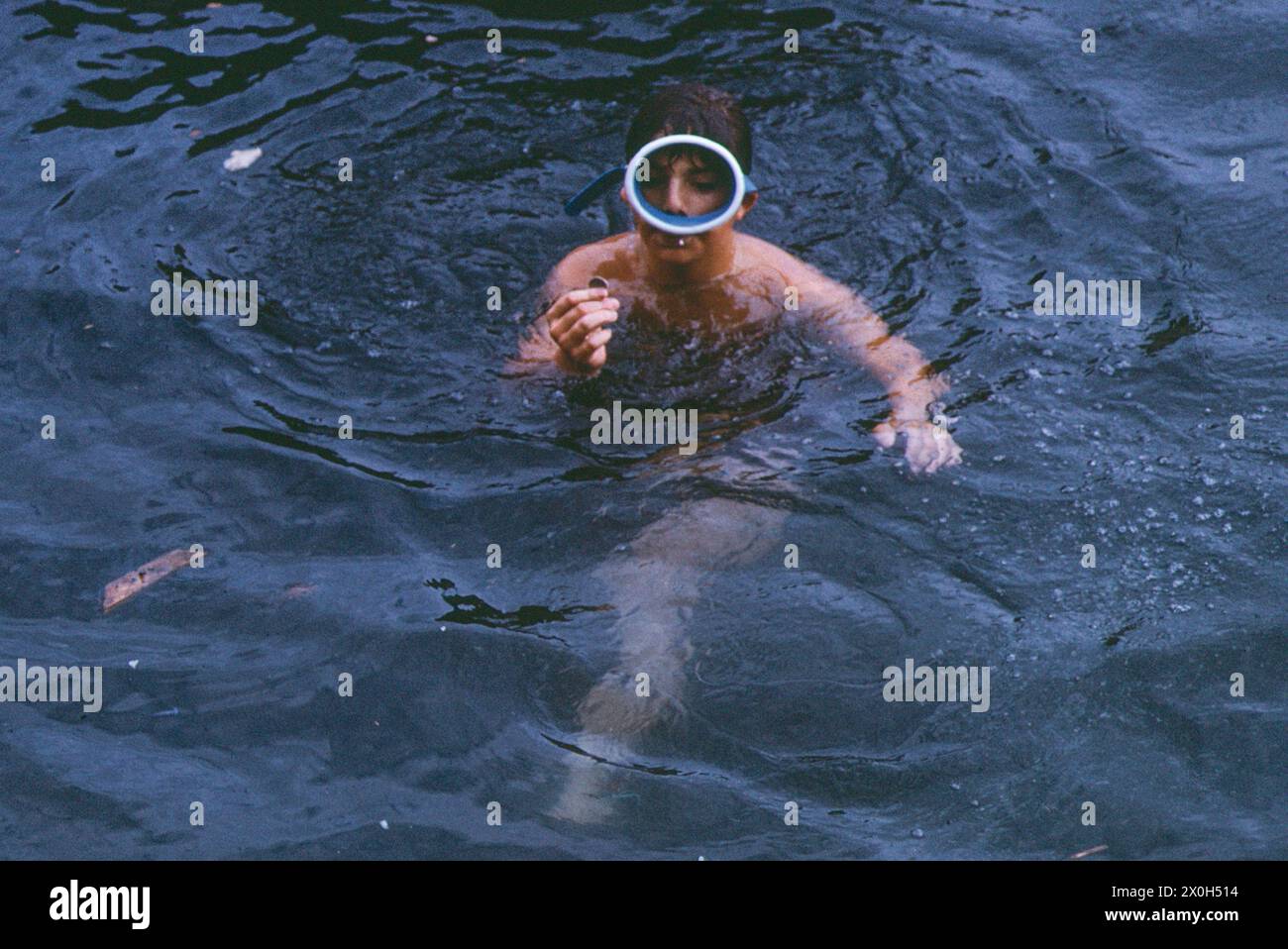 Swimming in the harbor basin with diving goggles, the boy tries to dive ...
