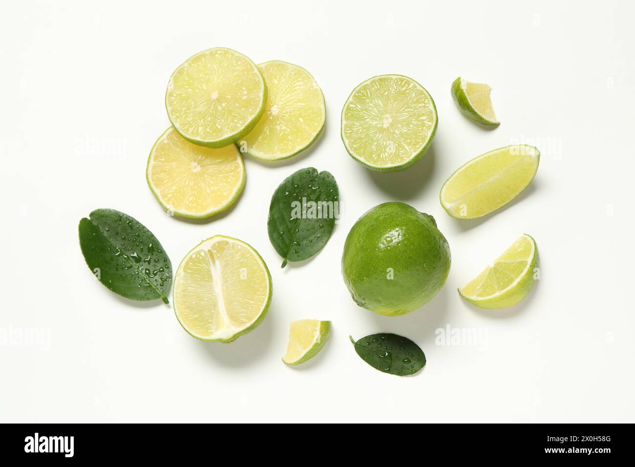 Whole and cut fresh ripe limes with green leaves on white background ...