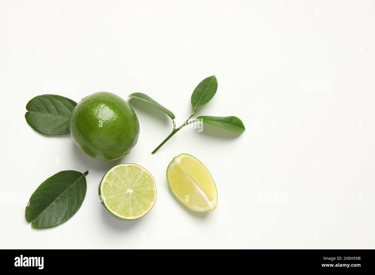 Whole and cut fresh ripe limes with green leaves on white background ...