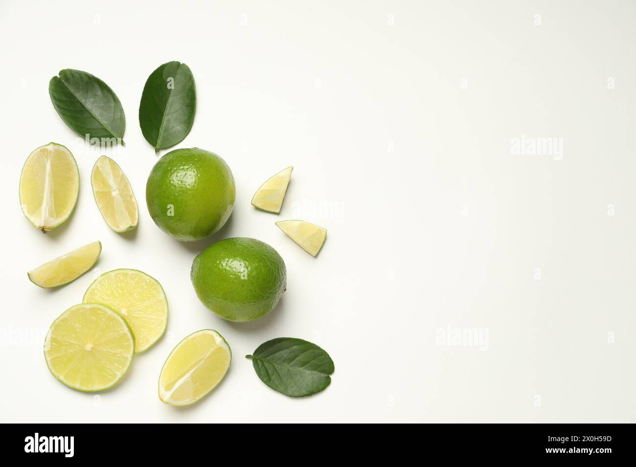 Whole and cut fresh ripe limes with green leaves on white background ...