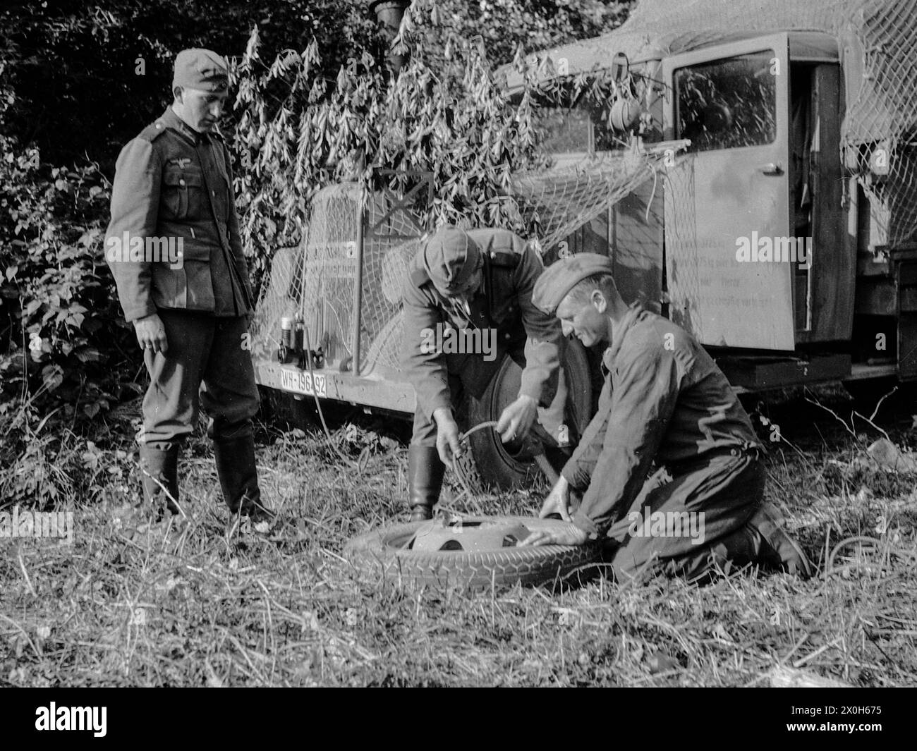Three Wehrmacht soldiers pumping up a repaired wheel with the help of a ...