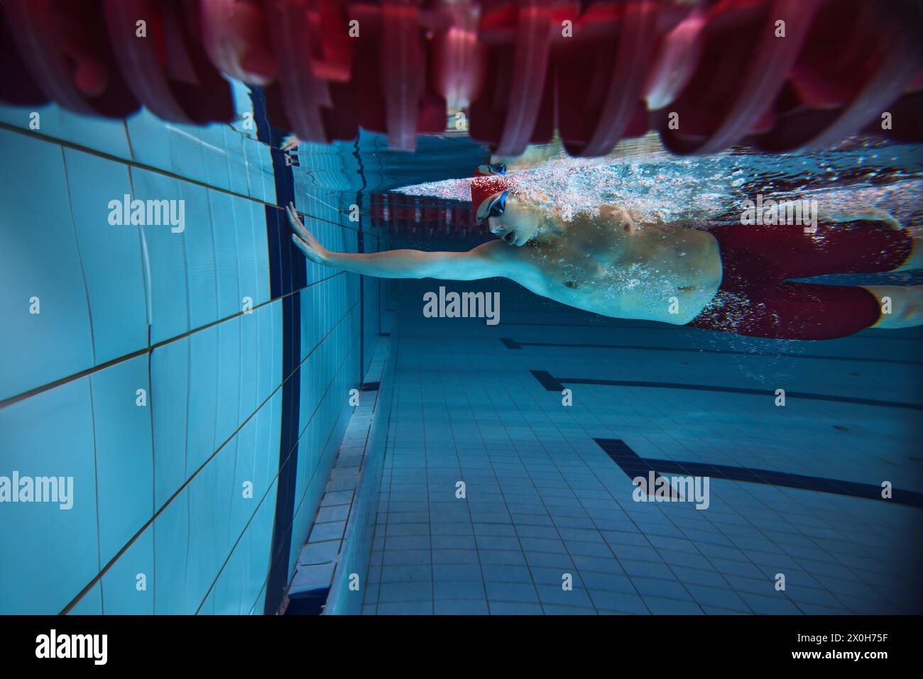 Underwater view of swimmer in red cap reaching edge of pool. Young man ...
