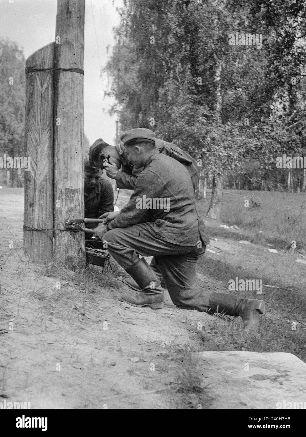 Three soldiers check the telephone connection on a telegraph pole. The ...