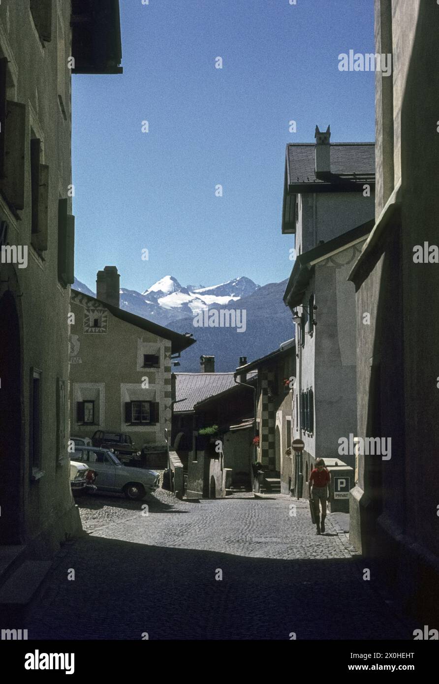 A street in the village with typical Engadine-style houses and parked ...