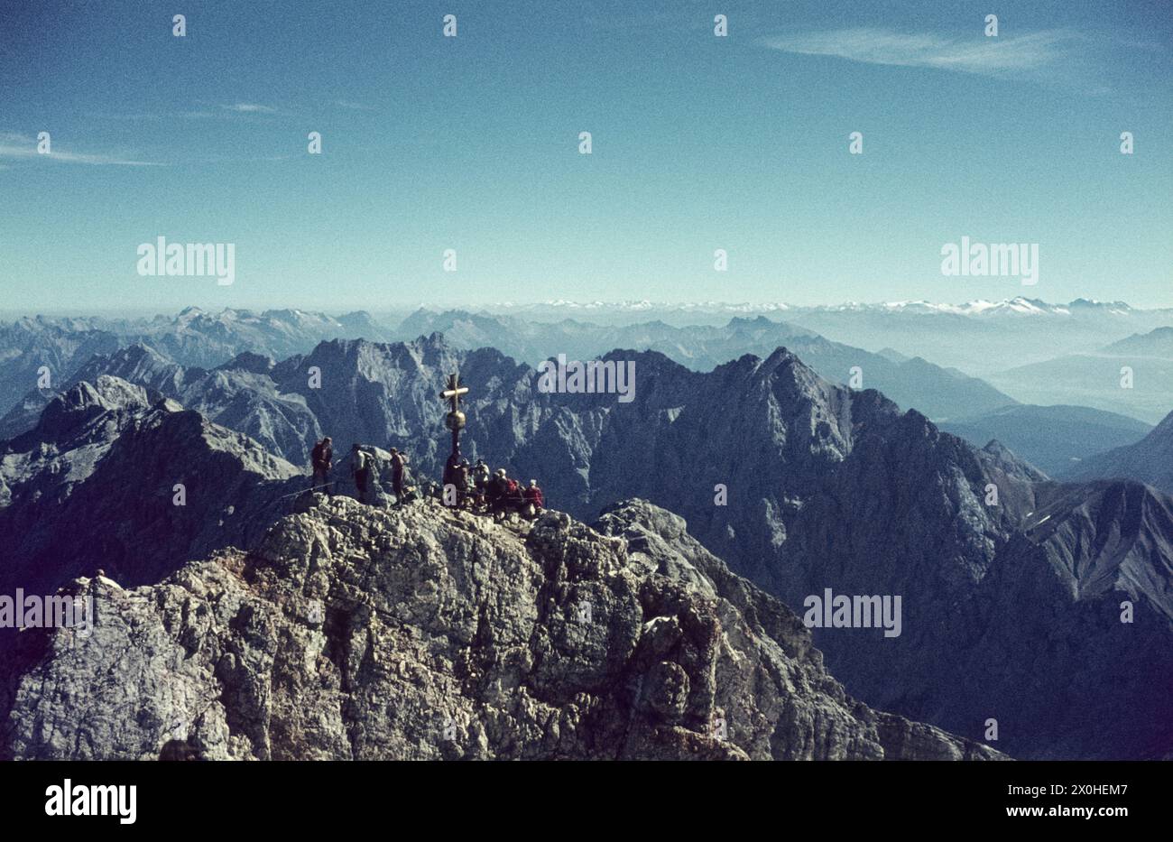 On the eastern summit, hikers stand around the summit cross.panorama on ...
