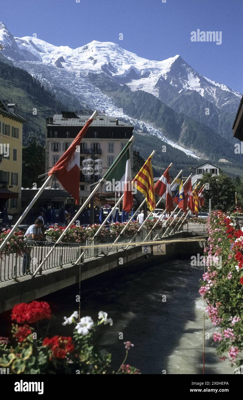 Colorful flags and boxes with geraniums are attached to the railing of ...