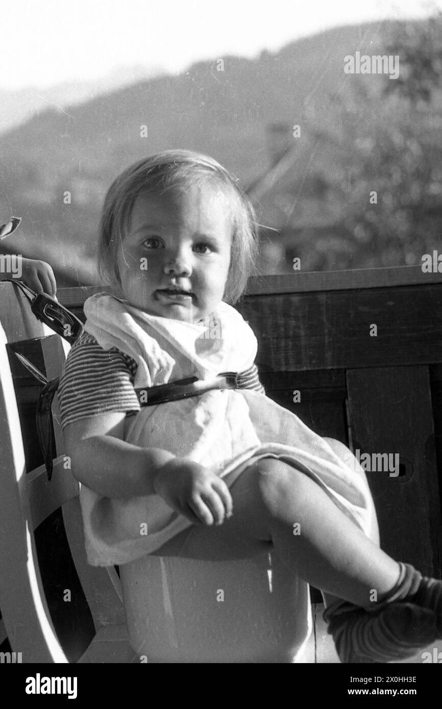 A toddler on the potty on a balcony looks into the camera. [automated ...